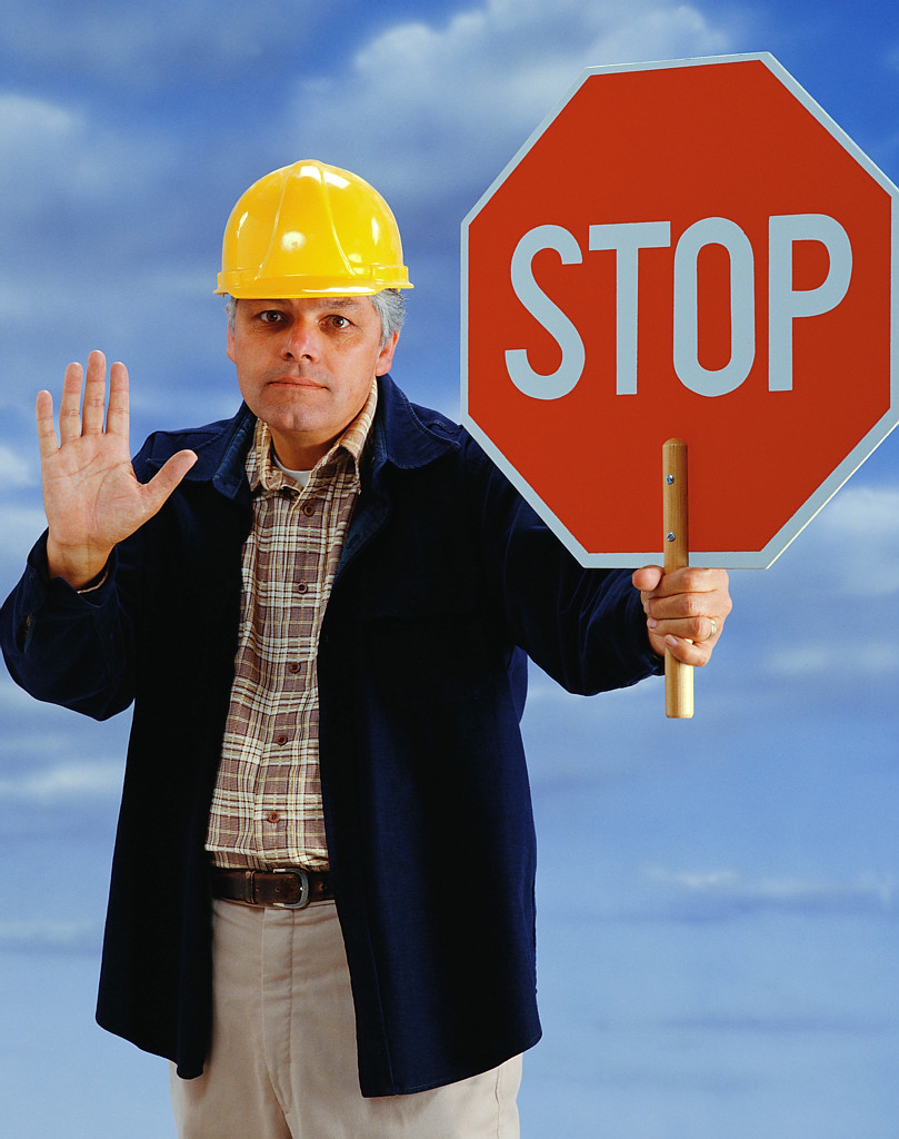 A Man In A Yellow Safety Hat Holding Up His Hand and Holding A Sign ...